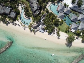 Vista aérea de um resort com várias bangalôs sobre a água, uma área de piscina central e uma praia.