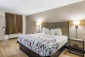 Quarto de hotel com uma cama grande, duas mesas de cabeceira, um criado-mudo, uma luminária na parede e uma janela com cortinas.
