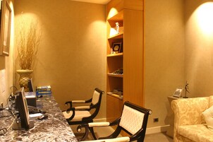 Quarto com escrivaninha de mármore, duas cadeiras, estante, abajur e sofá.