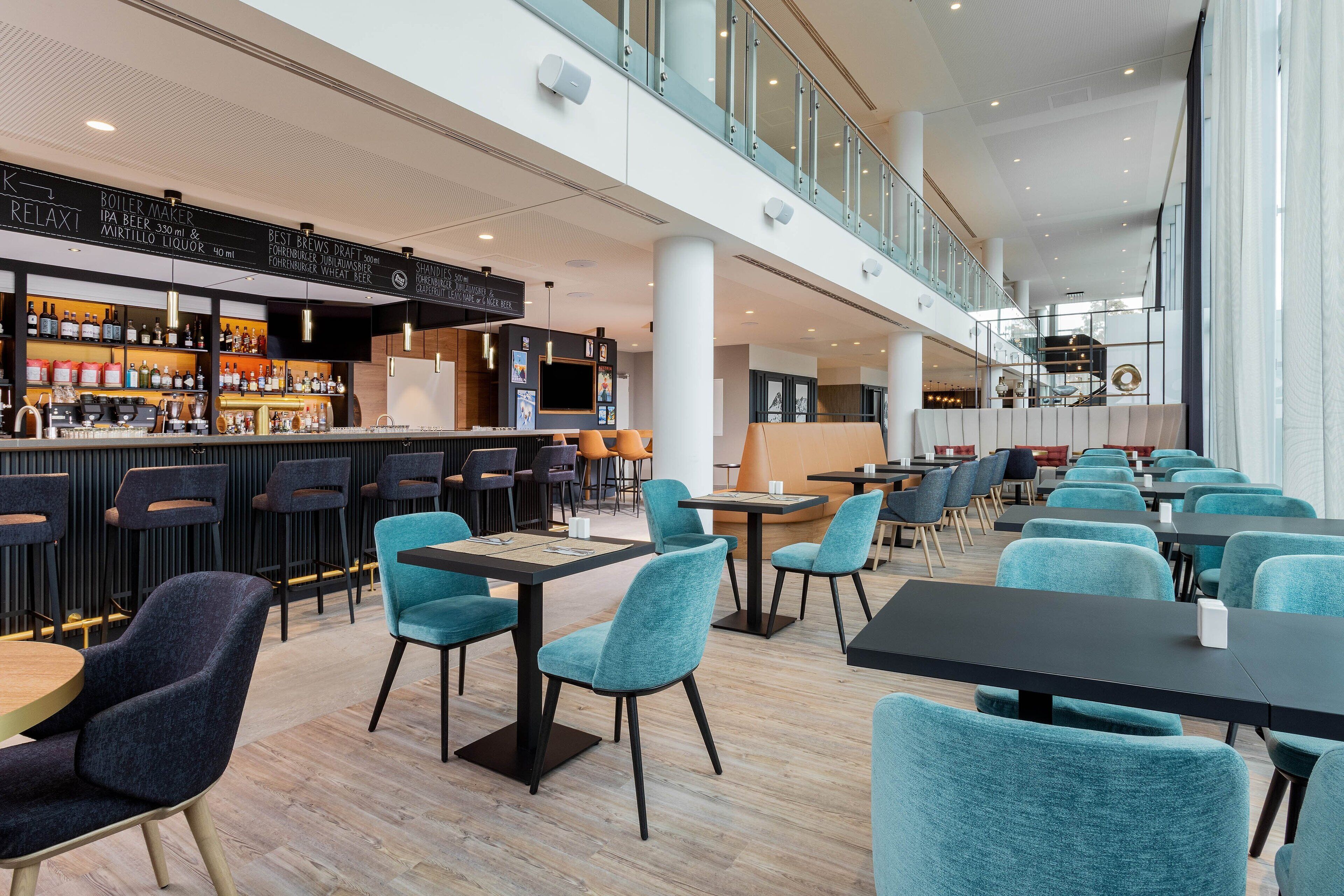 Um lobby moderno de hotel com área de bar, disposição de assentos e teto alto com guarda-corpos de vidro.