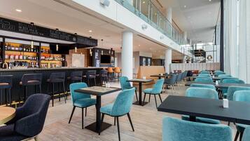 Um lobby moderno de hotel com área de bar, disposição de assentos e teto alto com guarda-corpos de vidro.