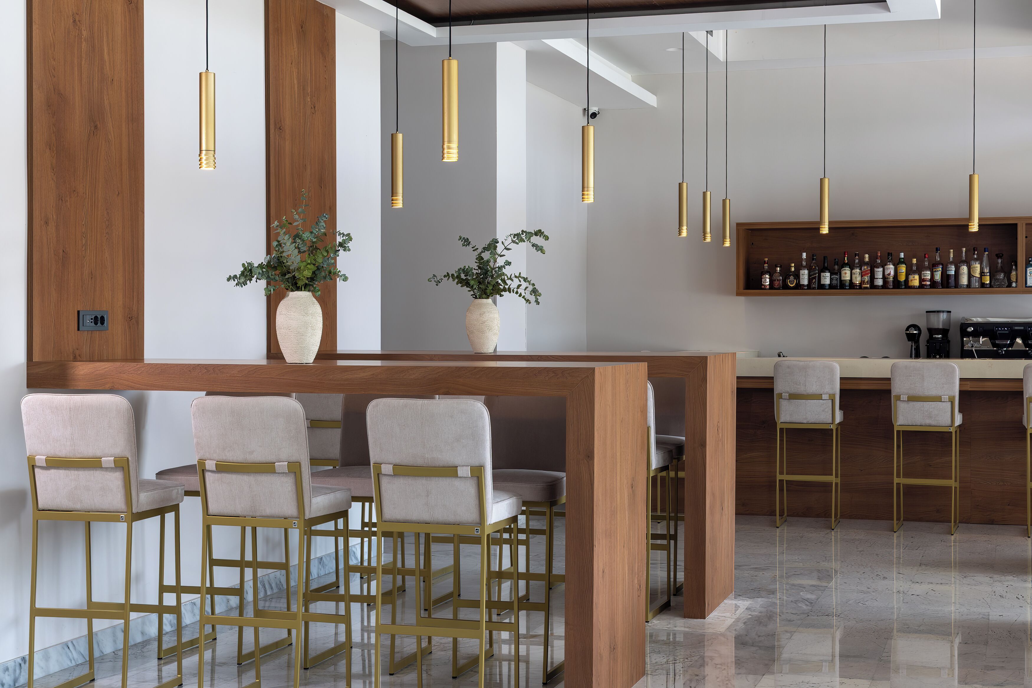 Uma área de bar moderna com detalhes em madeira, banquetas, luminárias pendentes e um espaço para vinhos.
