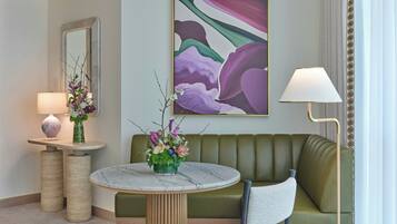 Um quarto com uma mesa redonda de mármore, um sofá, um abajur, um espelho e uma obra de arte floral na parede.