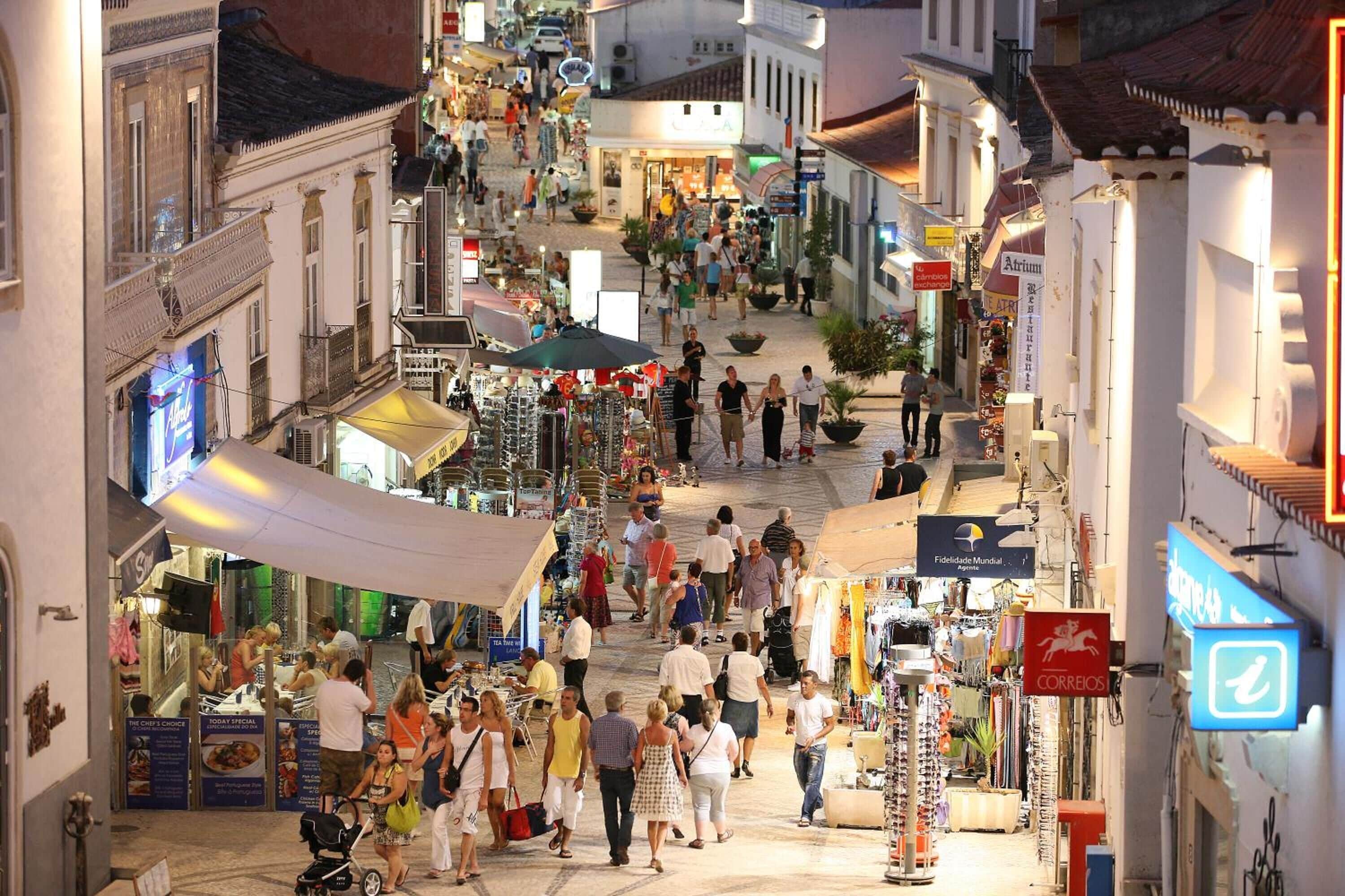 Cena movimentada de rua com lojas e pedestres.