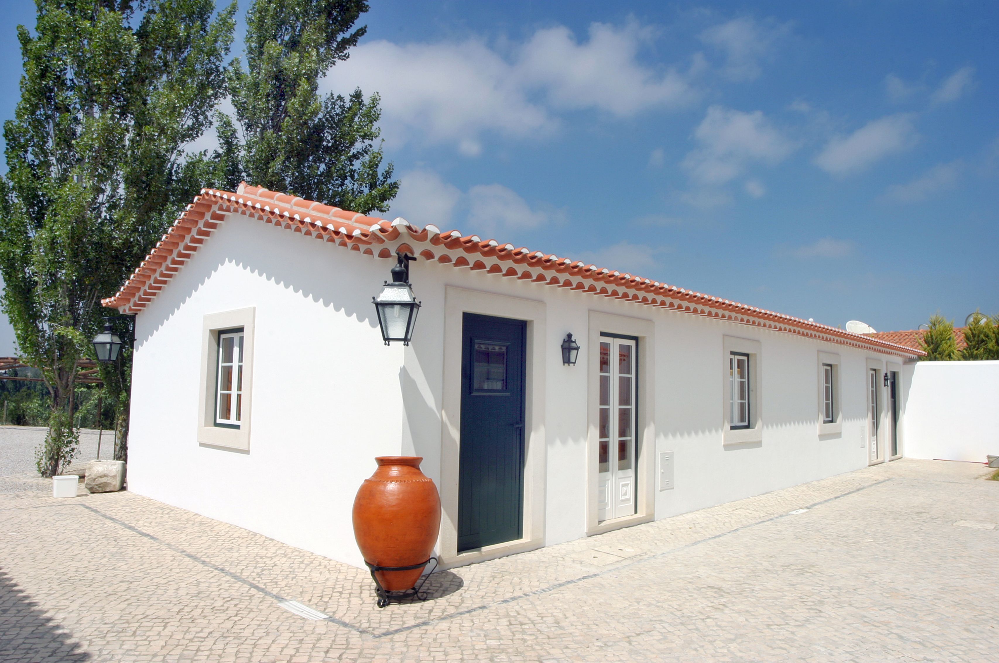 Um edifício branco com telhado de telhas vermelhas, uma porta azul e um grande vaso de terracota em frente.