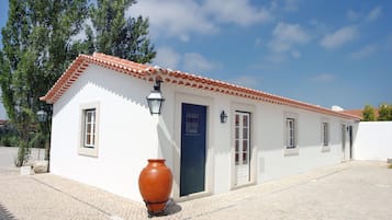 Um edifício branco com telhado de telhas vermelhas, uma porta azul e um grande vaso de terracota em frente.