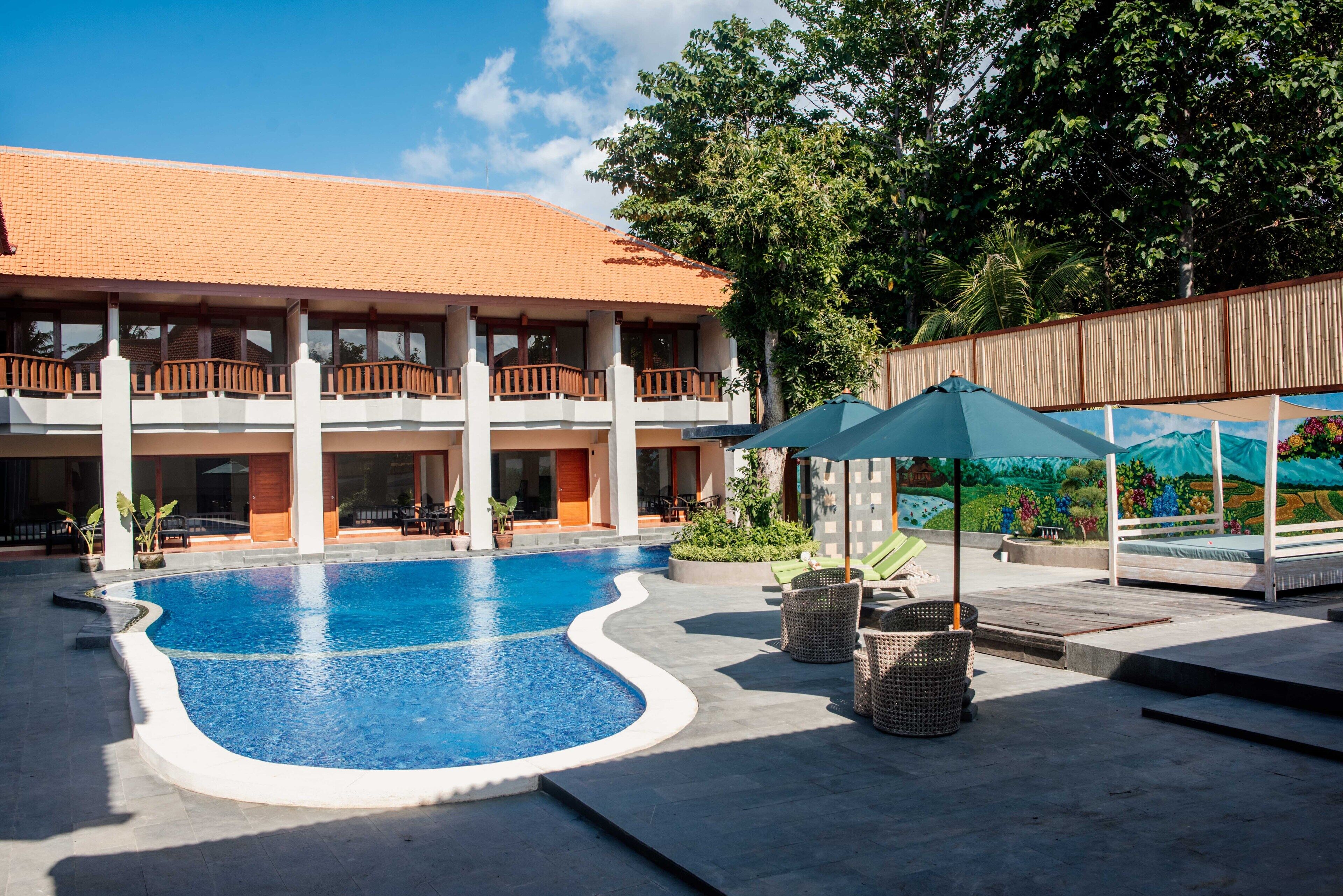 Uma piscina com borda ondulada, cercada por espreguiçadeiras e uma área de estar coberta.