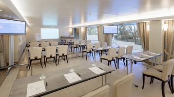 Sala de conferências com várias mesas e cadeiras, equipada com telas e materiais de apresentação.