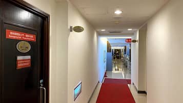 Corredor de hotel com tapete vermelho, placas de saída de emergência e sinalização para sauna masculina.