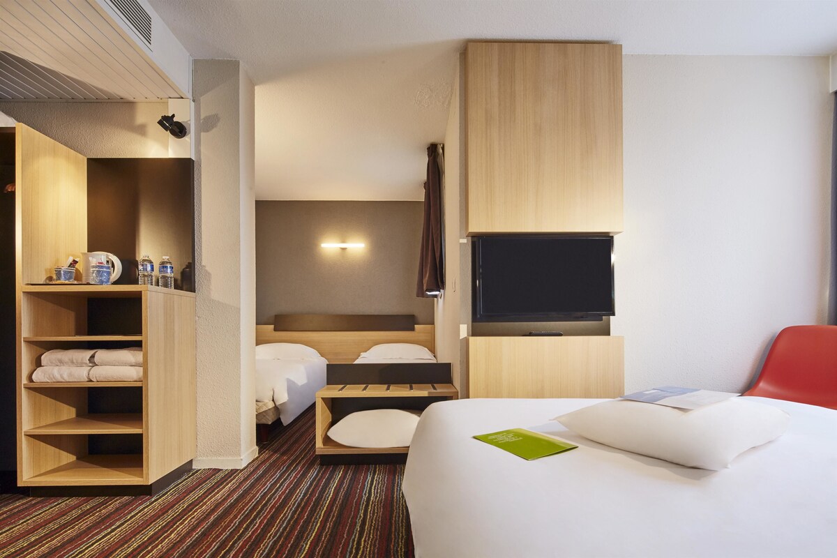 Quarto de hotel com uma cama grande, um guarda-roupa de madeira, uma televisão de tela plana e uma cadeira vermelha.