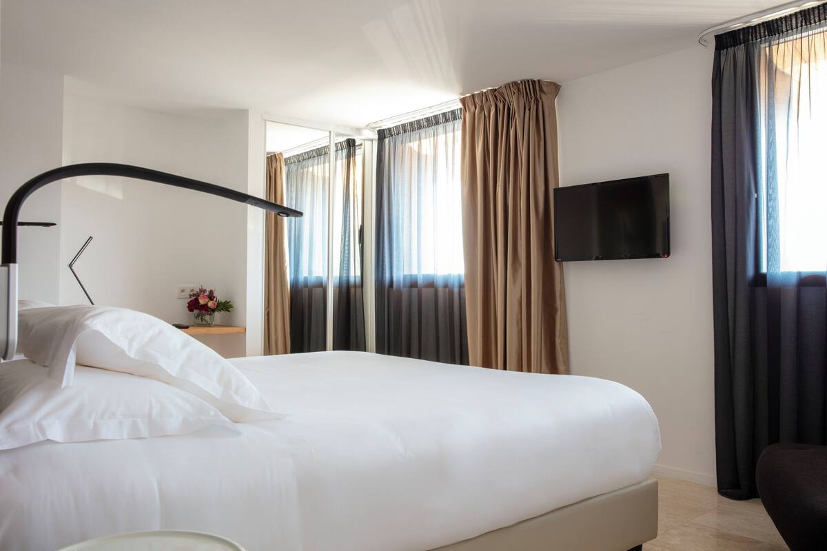 Quarto de hotel com uma cama, televisão e cortinas.