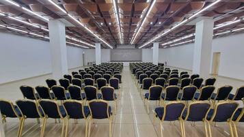 Uma sala de conferências grande e vazia, com fileiras de cadeiras e teto alto com vigas aparentes.