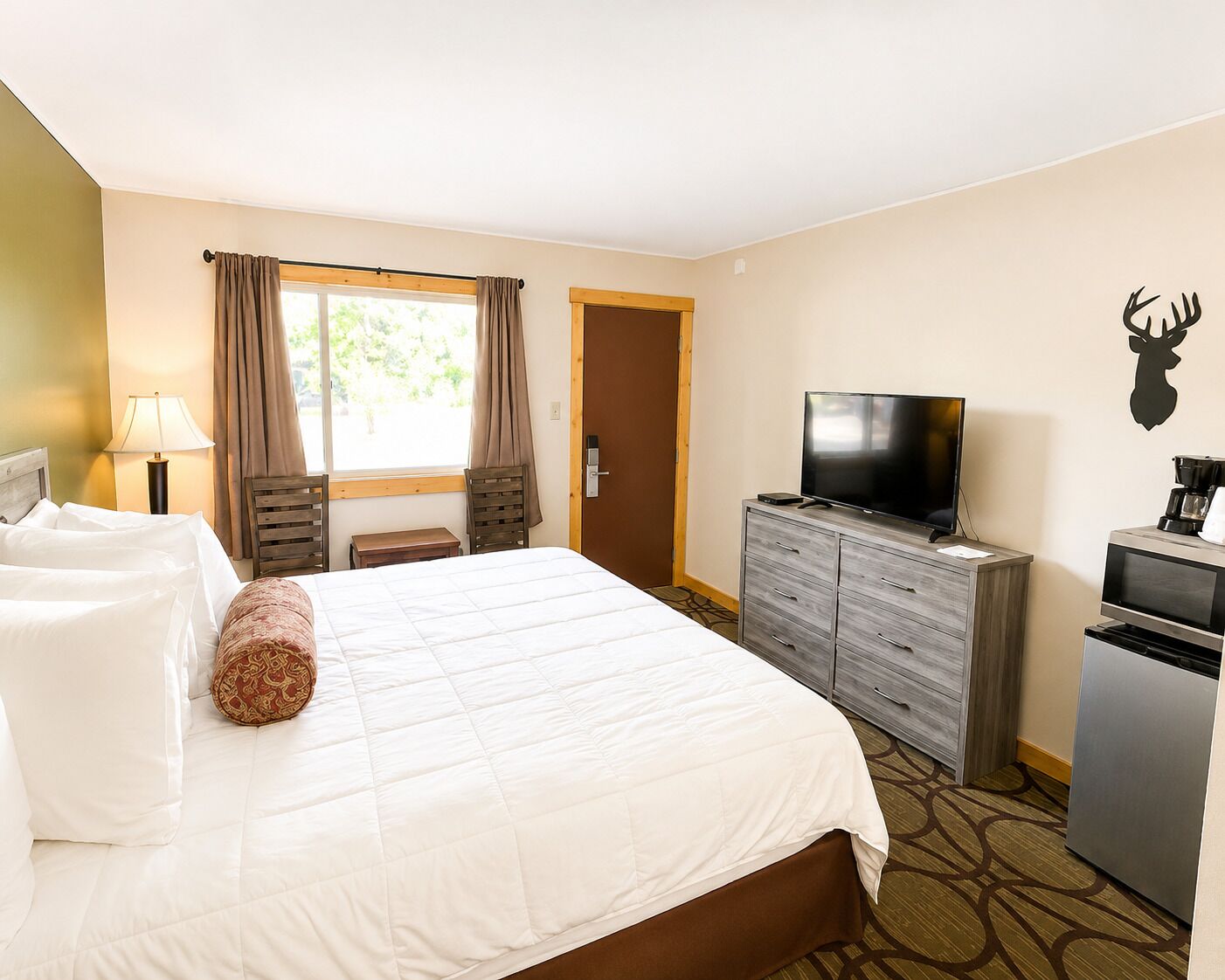 Quarto de hotel com cama, televisão, escrivaninha com cafeteira e um chifre de veado fixado na parede.