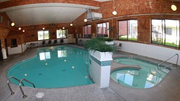 Piscina interior com deck revestido em azulejo, área de jardim pequena e parede de tijolos.