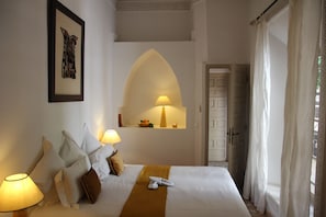 Quarto de hotel com cama, travesseiros, luminária, quadro emoldurado e porta.