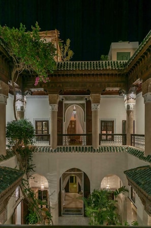 Pátio com um arco central, cercado por colunas e arcos, com vista para um quarto através do arco.