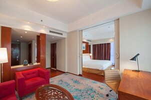 Quarto de hotel com sofá vermelho, mesa de madeira, cadeira de rodas e cama com vista do quarto.