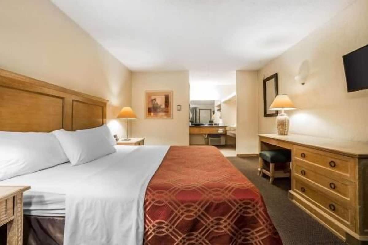 Quarto de hotel com cama, escrivaninha, cadeira, cômoda e televisão na parede.