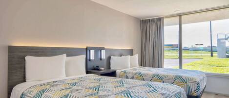 Quarto de hotel com duas camas, uma mesa de cabeceira e uma janela grande com vista para o exterior.