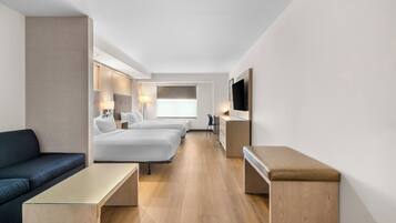 Quarto de hotel com cama, sofá, escrivaninha, televisão e janela.