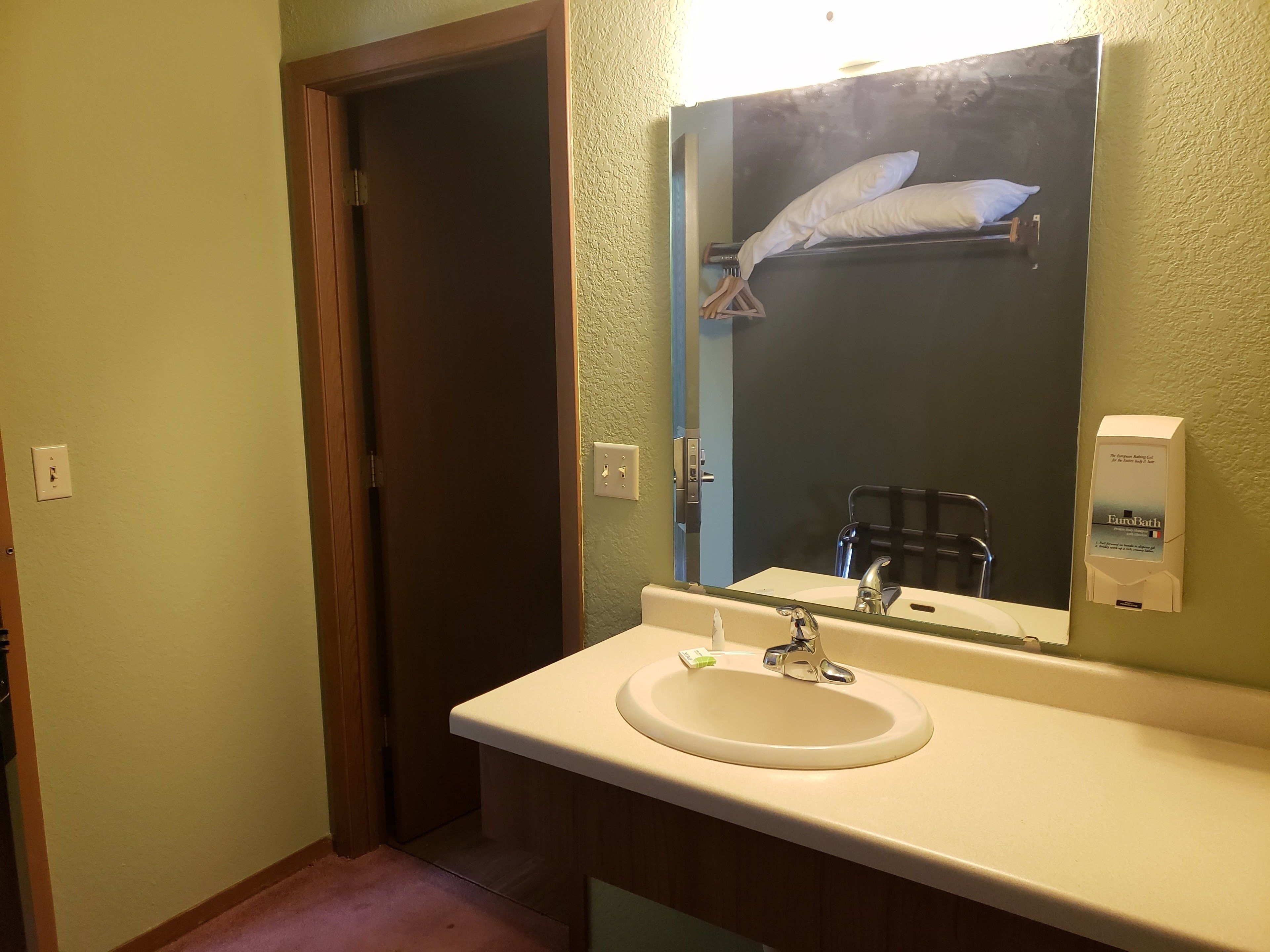 Casa de banho com lavatório branco, espelho, porta-toalhas e dispensador de gel desinfetante.