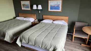 Quarto de hotel com duas camas, uma mesa de cabeceira com telefone e luminária, uma cadeira e duas quadros na parede.