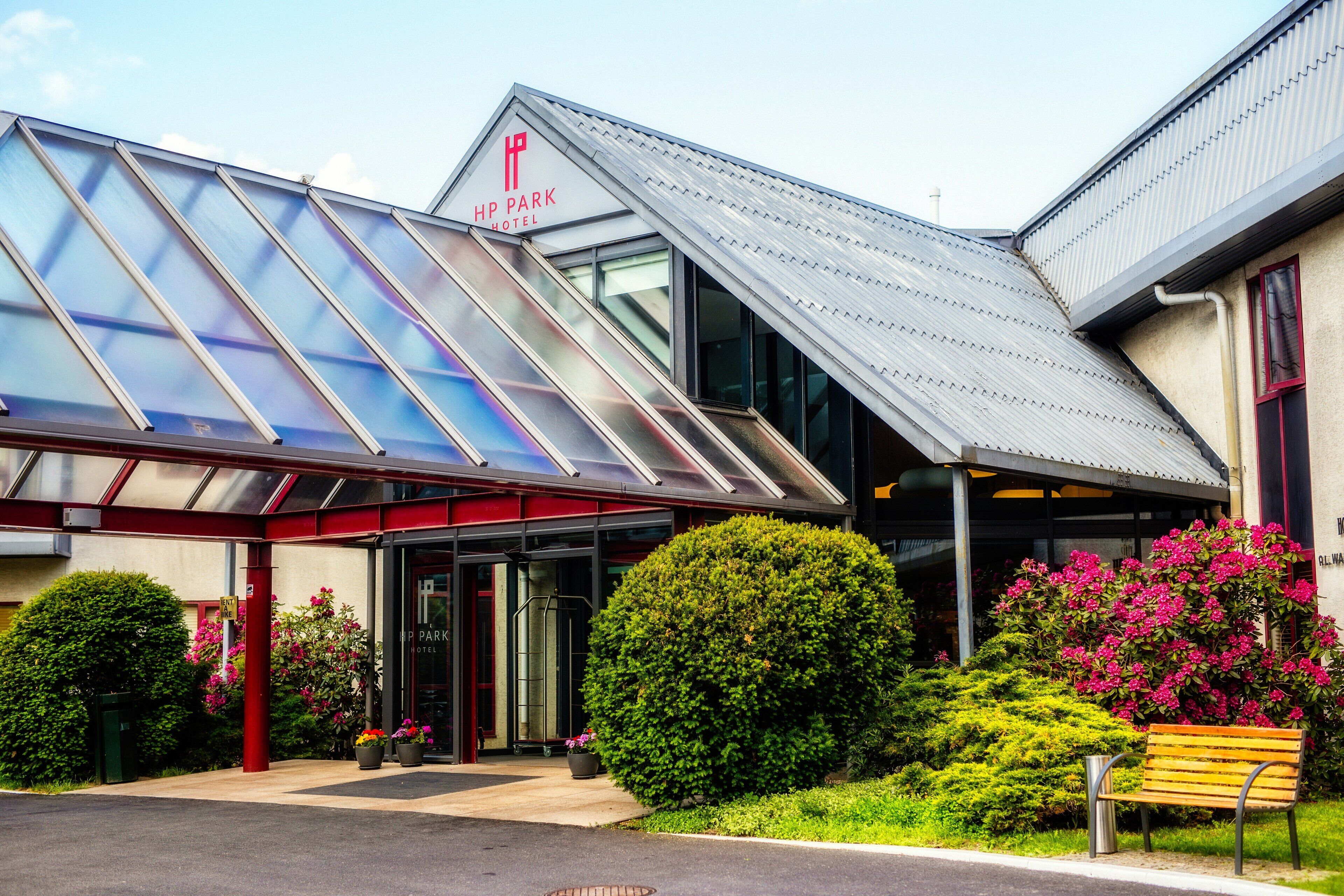 Exterior do Hotel HP Park, com design moderno, incluindo entrada em vidro e uma galeria coberta.