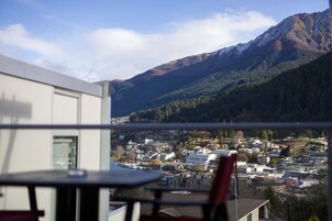 Varanda com mesa e cadeiras, vista para uma cidade e montanhas.