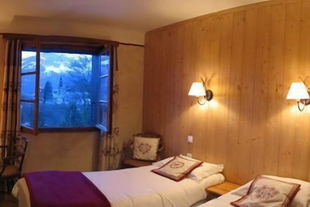 Um quarto com painéis de madeira, uma cama, duas mesas de cabeceira, uma cadeira e uma escrivaninha.