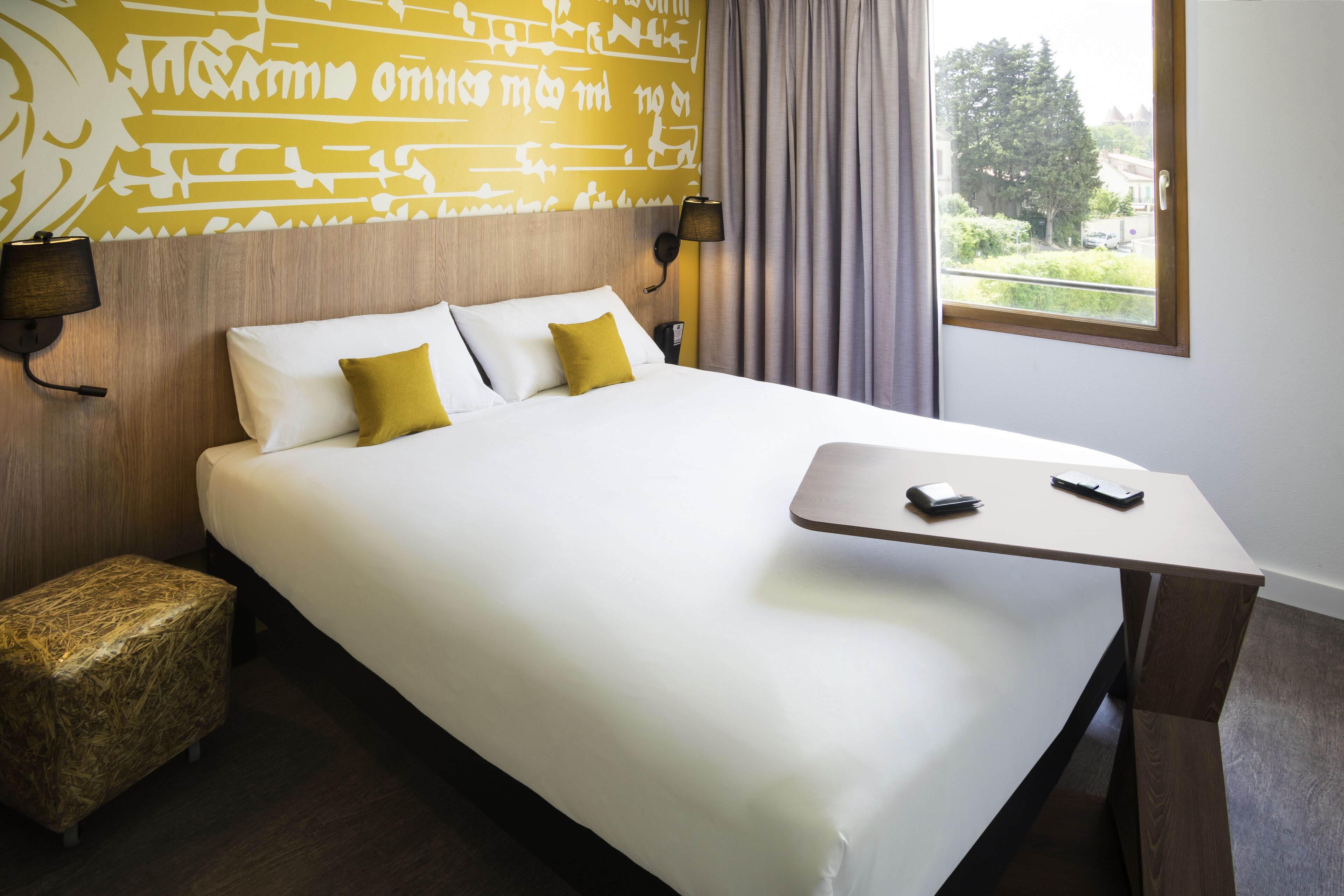 Quarto de hotel com uma cama grande, uma mesa pequena e vista para o exterior.