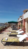 Terraço no telhado com espreguiçadeiras, um espaço de estar coberto e plantas em vasos.