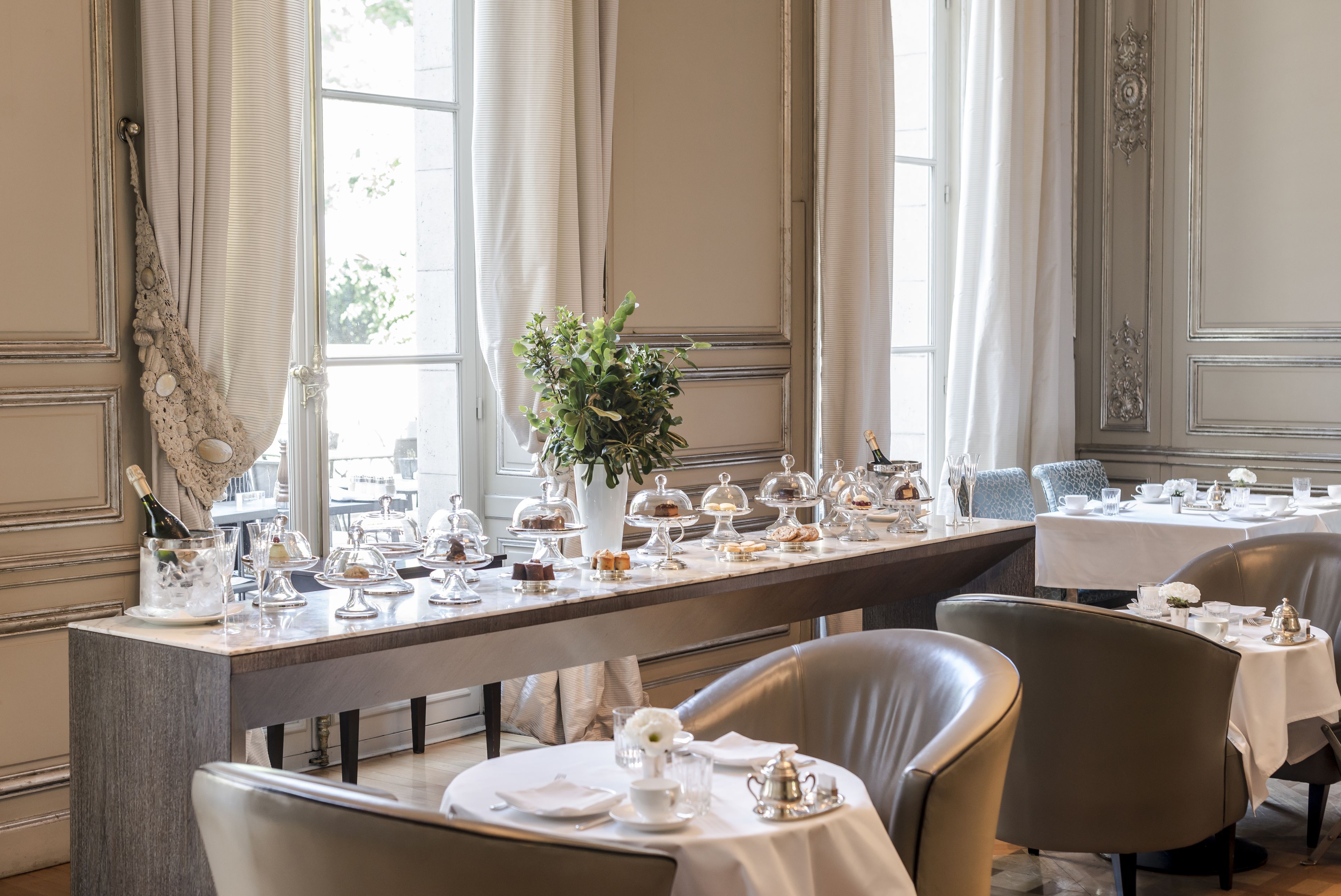 Uma sala de jantar formal com uma mesa comprida posta para refeição, cadeiras elegantes e um arranjo de plantas decorativo.