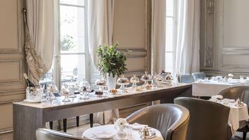 Uma sala de jantar formal com uma mesa comprida posta para refeição, cadeiras elegantes e um arranjo de plantas decorativo.