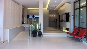 Um hall moderno com balcão de atendimento, duas televisões, uma parede de vidro e uma área de estar vermelha.