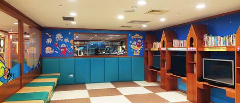 Espaço de recreação infantil com piso xadrez, assentos e balcão com mural de personagem de desenho animado.