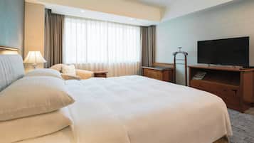 Quarto de hotel com uma cama grande, televisão, escrivaninha e uma cadeira.