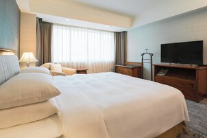 Quarto de hotel com uma cama grande, televisão, escrivaninha e uma cadeira.