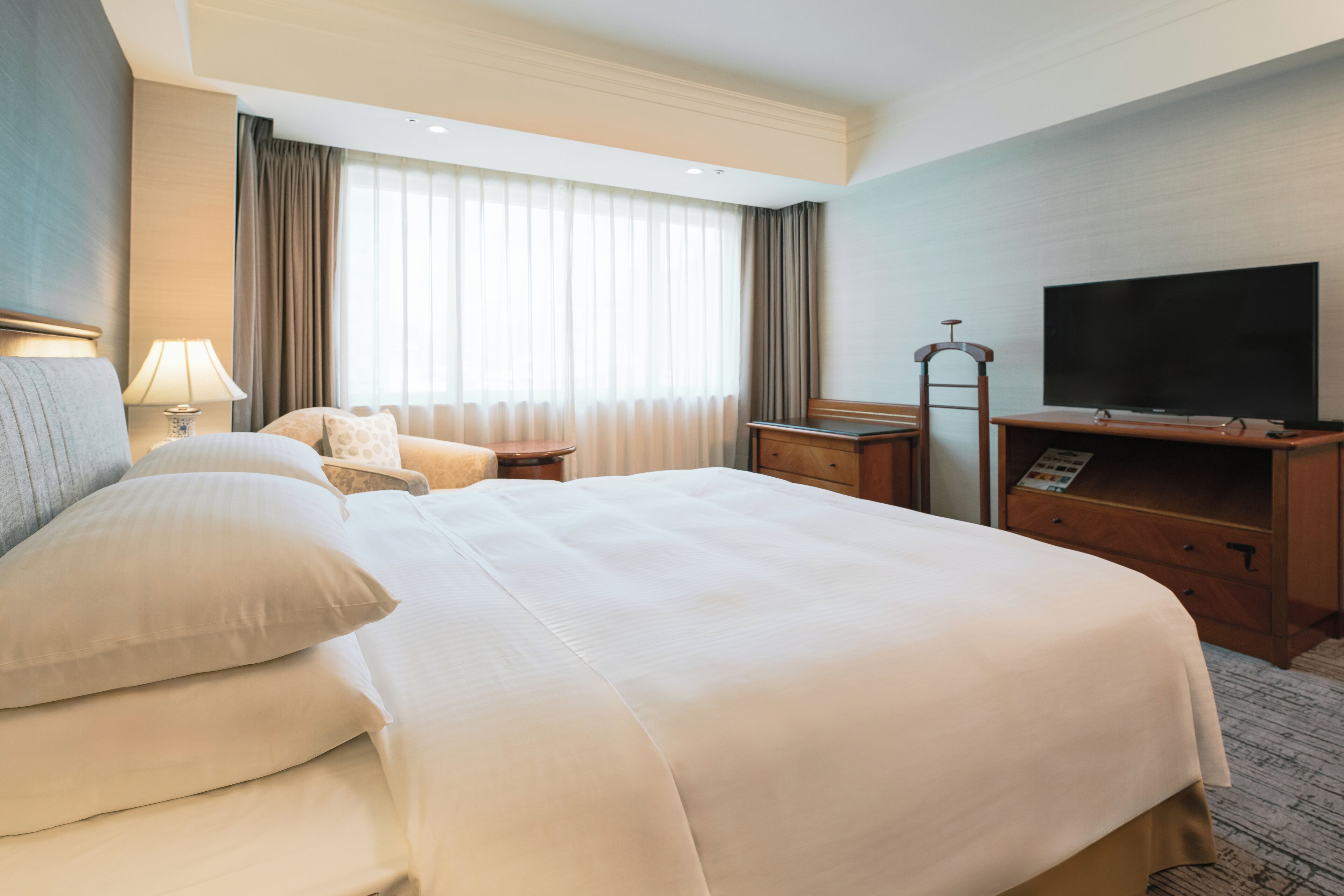 Quarto de hotel com uma cama grande, televisão, escrivaninha e uma cadeira.