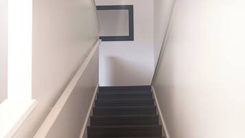 Uma escadaria com degraus escuros e corrimãos brancos, que leva a um patamar com um espelho emoldurado a preto.