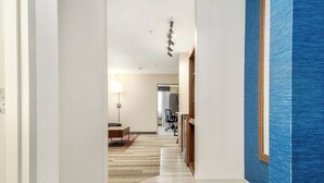 Um corredor de hotel com piso de madeira, uma mesa com cadeira, uma luminária e uma parede azul decorativa.