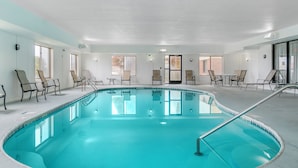 Uma grande piscina interior com espreguiçadeiras e mesas ao redor da borda.
