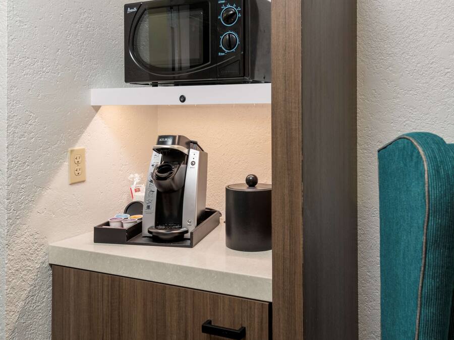 Uma cozinha compacta com micro-ondas, cafeteira e um pequeno armário.