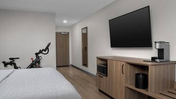 Quarto de hotel com cama, armário de madeira com micro-ondas, bicicleta e televisão de tela plana na parede.