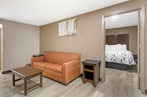 Quarto de hotel com sofá, mesa pequena, mesa de cabeceira e cama com colcha estampada.