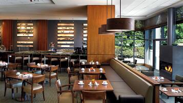 Um restaurante com várias áreas de estar, incluindo cabines e mesas, uma janela grande e uma lareira.