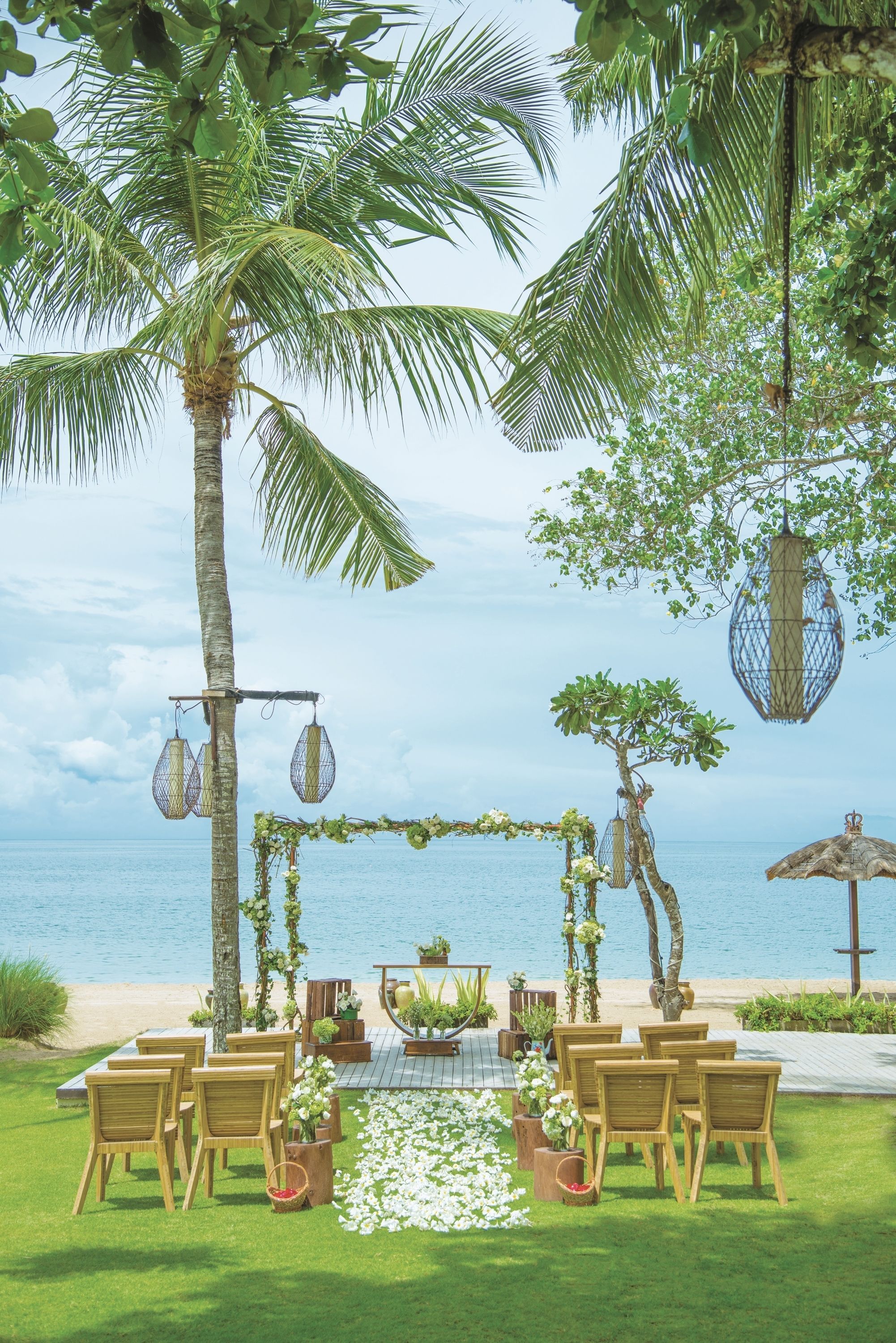 Montagem para um casamento tropical ao ar livre, com mesa de madeira, cadeiras e um arco decorativo.
