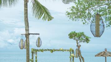 Montagem para um casamento tropical ao ar livre, com mesa de madeira, cadeiras e um arco decorativo.