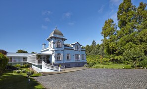 Um edifício grande e branco de dois andares, com uma torre e varanda coberta.