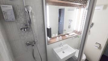 Uma casa de banho moderna com cabine de duche em vidro, lavatório branco e espelho a refletir o espaço.
