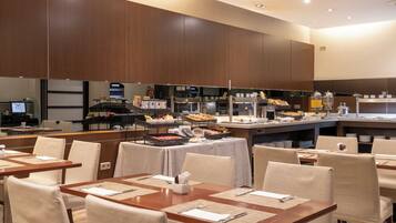 Espaço de refeições de hotel com opções de pequeno-almoço em estilo buffet, disposição de mesas e um canto para café.